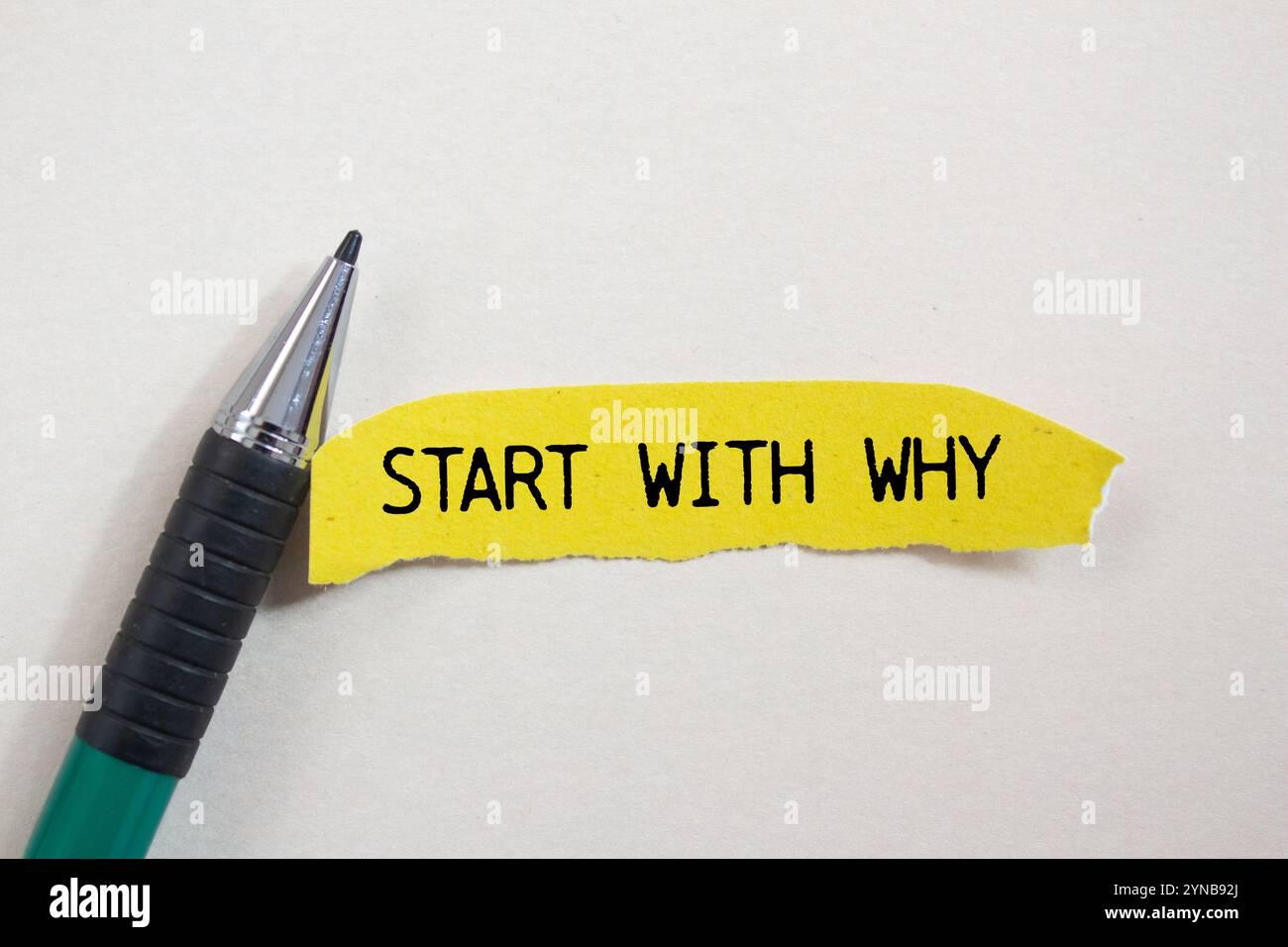 Start with why message written on ripped torn yellow paper piece and a pen with white background ...