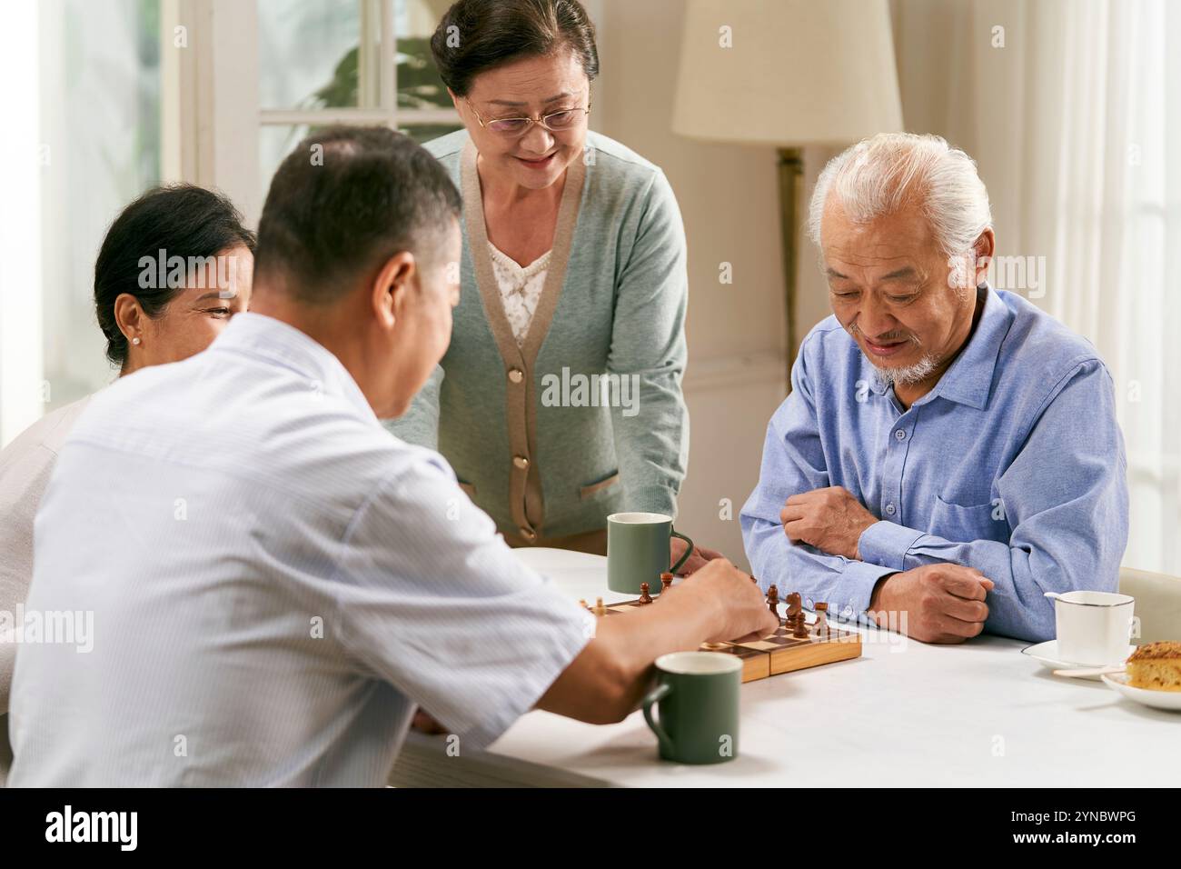 group of happy asian senior people two couples gathering at home playing chess game together ...