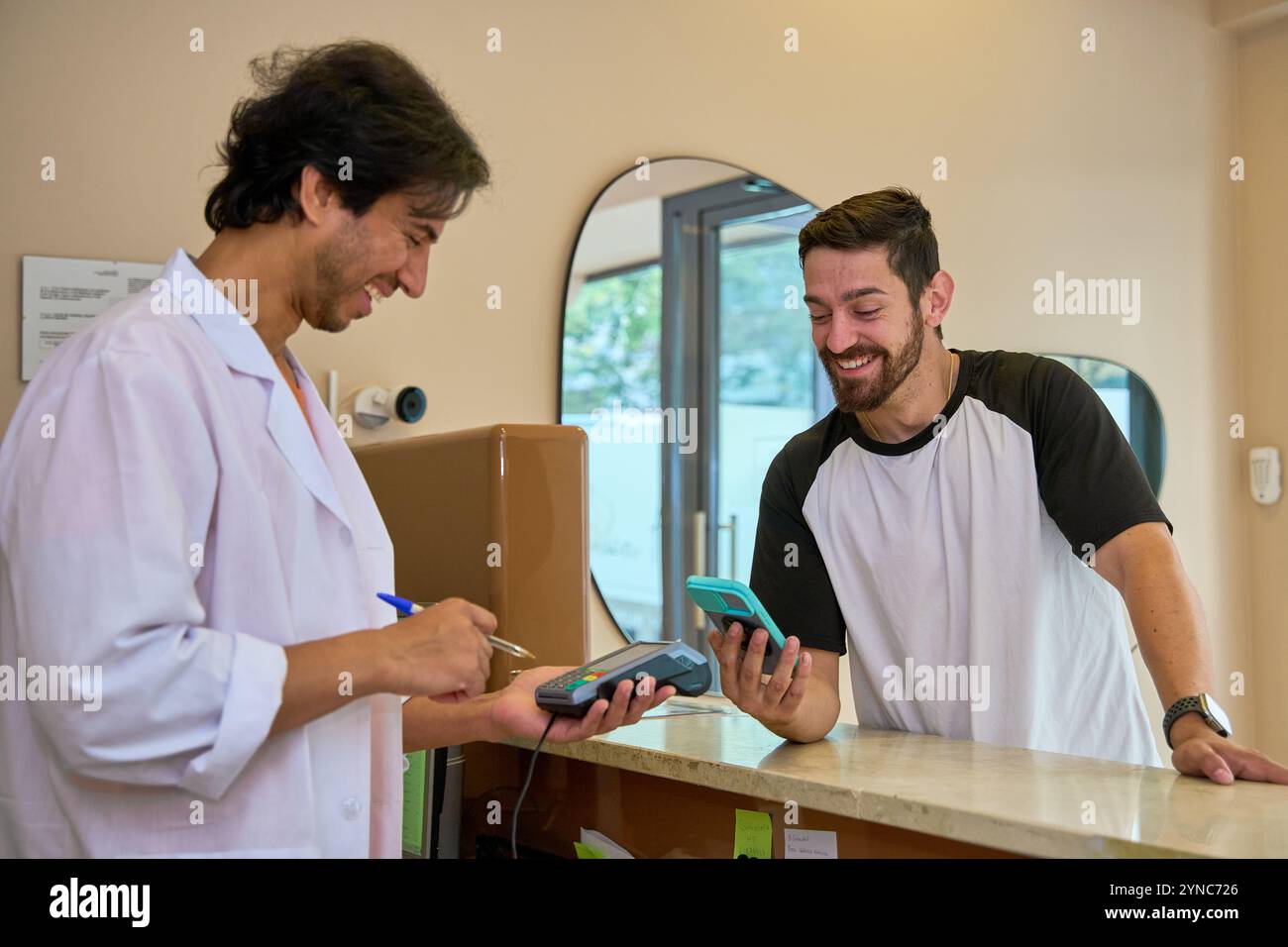 A doctor and patient share a friendly moment while processing a payment ...