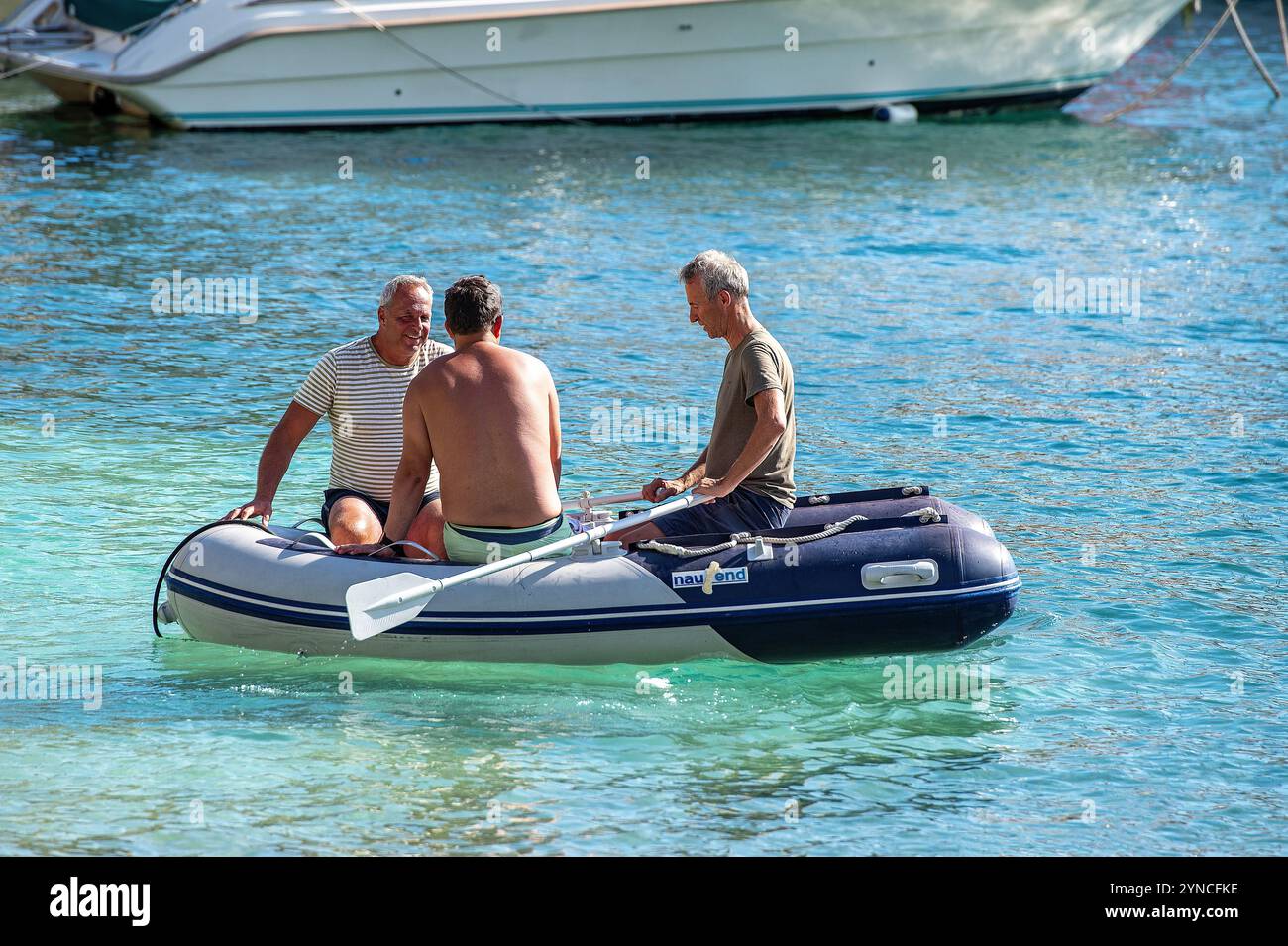 three men in a small rubber inflatable dinghy rowing ashore from a ...
