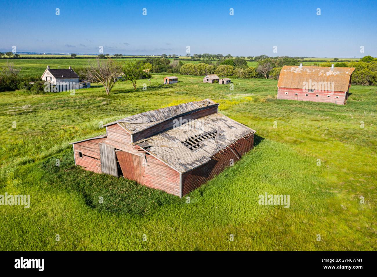 A barn with a broken roof sits in a field. The barn is surrounded by ...