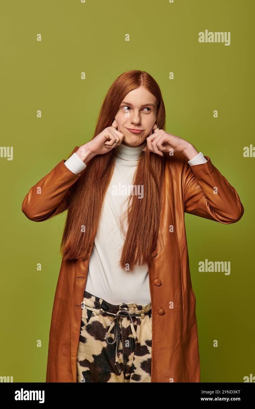 A young man with long red hair playfully pulls on his cheeks while ...