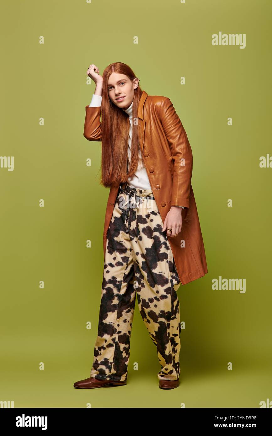 A young man with long red hair poses in unique attire against a green ...