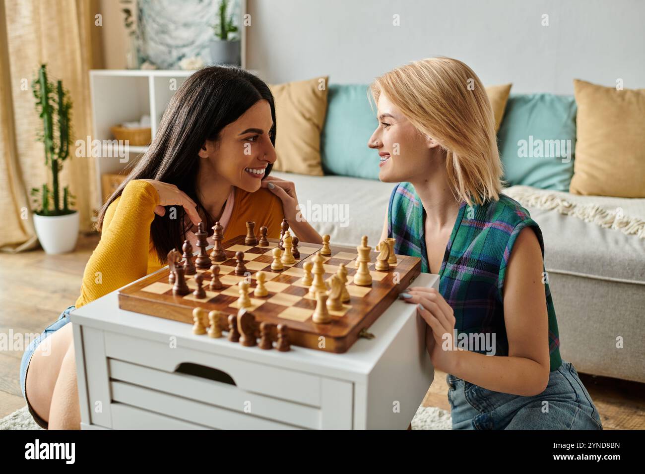 Two young women share smiles and laughter while playing chess together ...