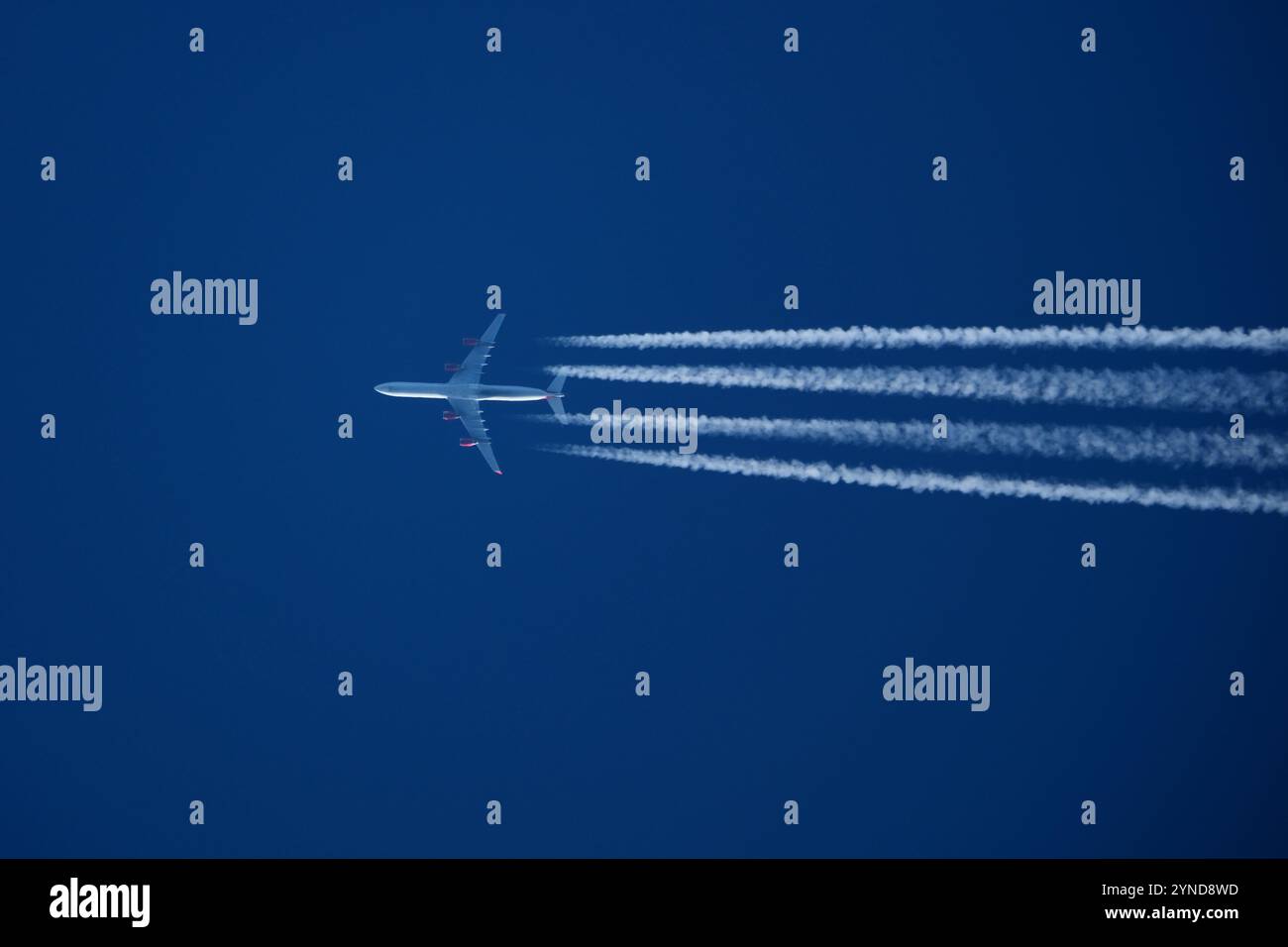 Four-engine airliner drawing a contrail in a clear blue sky Stock Photo ...