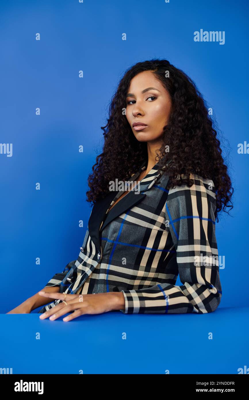 A confident woman in a chic checked outfit poses against a bright blue ...