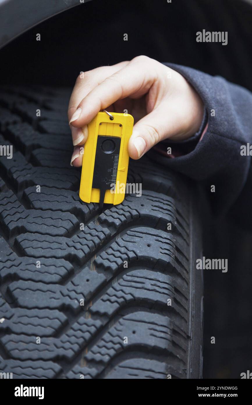 A blonde woman measures the tread depth of her car tyre. The right ...