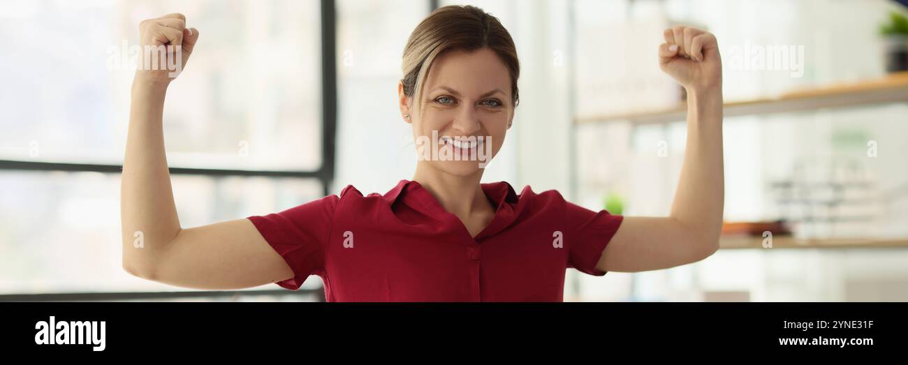 Smiling woman manager shows biceps muscles at workspace in company ...