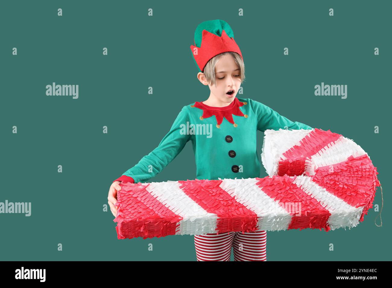 Cute shocked boy in elf costume with candy cane pinata on green ...