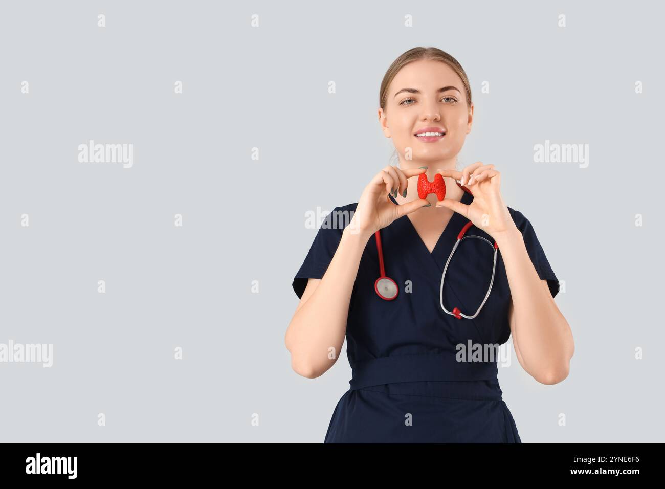 Female endocrinologist with thyroid gland model on grey background ...
