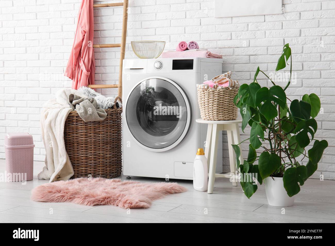 Modern washing machine, basket with laundry, houseplant and ladder in ...
