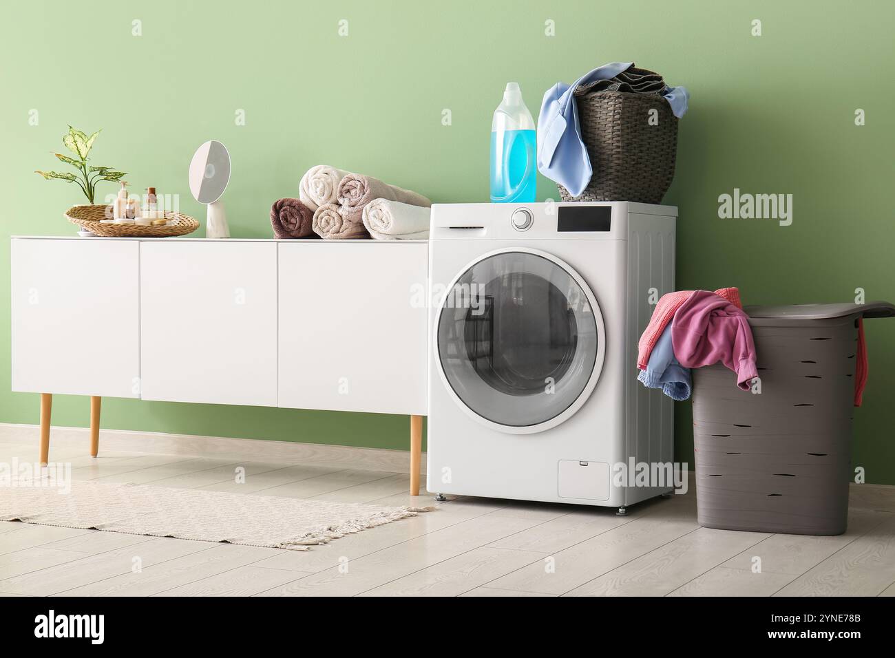 Modern washing machine, chest of drawers and basket with laundry in ...