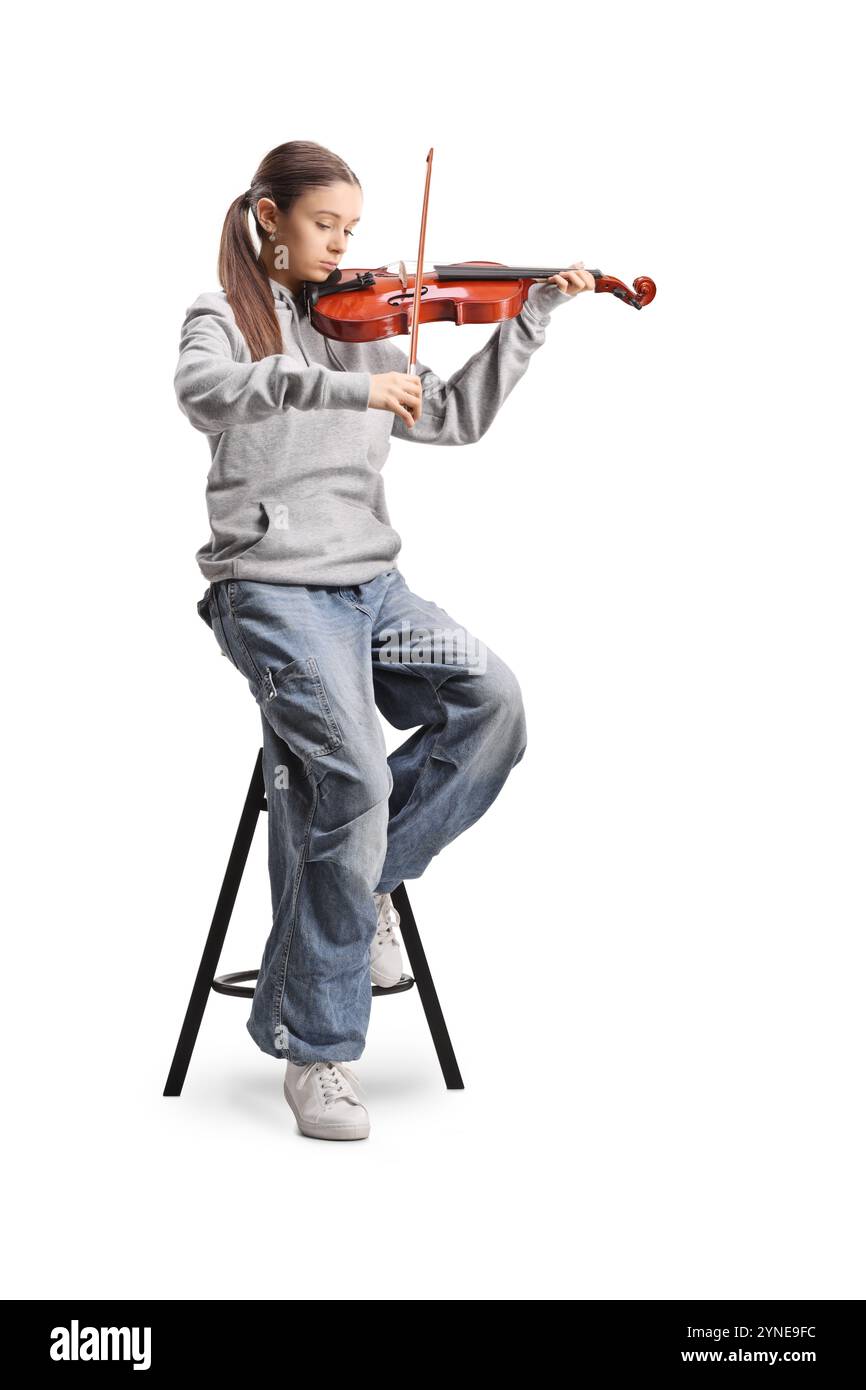 Teenage girl sitting on a chair and playing a violin isolated on white ...