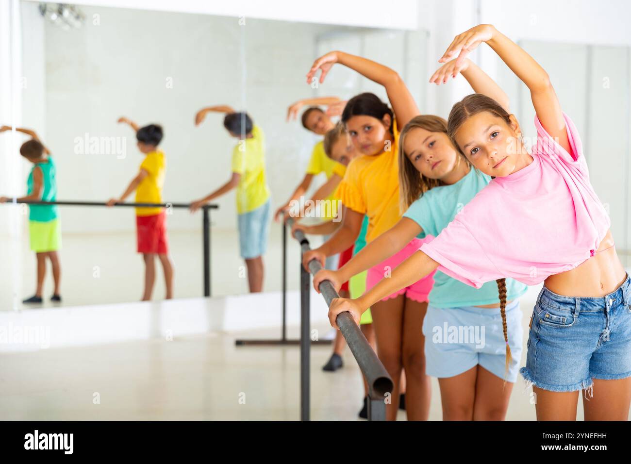 Assiduous preteen girl working near ballet barre during group ...