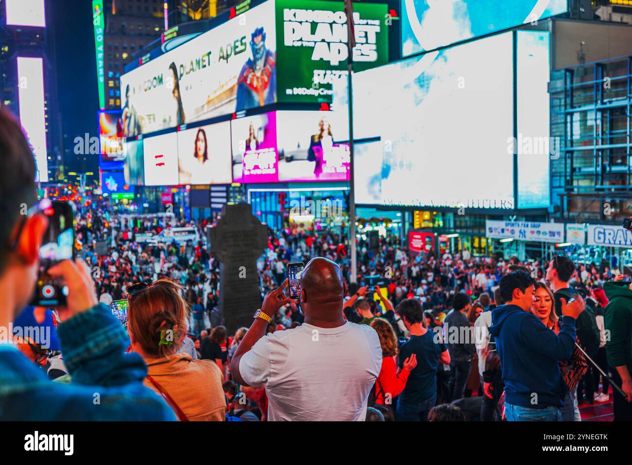 Crowds gather on illuminated red steps at Times Square surrounded by ...