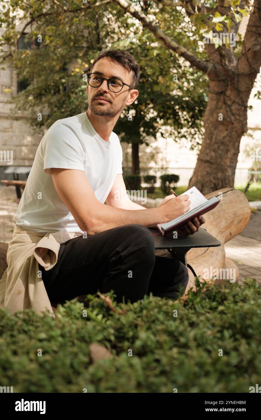 Young man writing in notebook while sitting on park bench Stock Photo ...