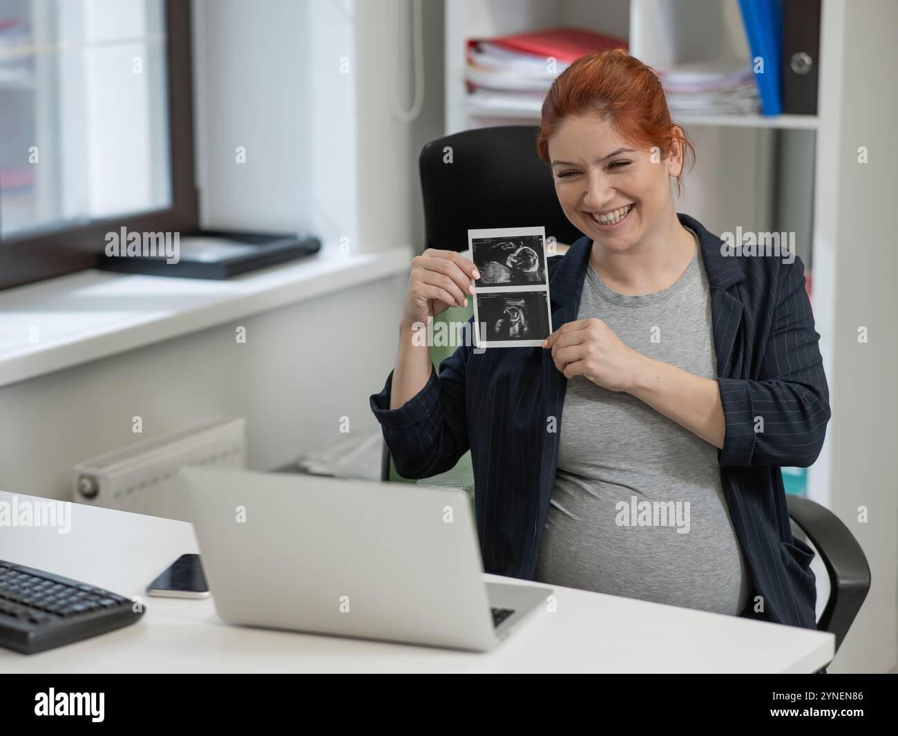 A pregnant woman shows a photo from an ultrasound scan of the fetus via ...