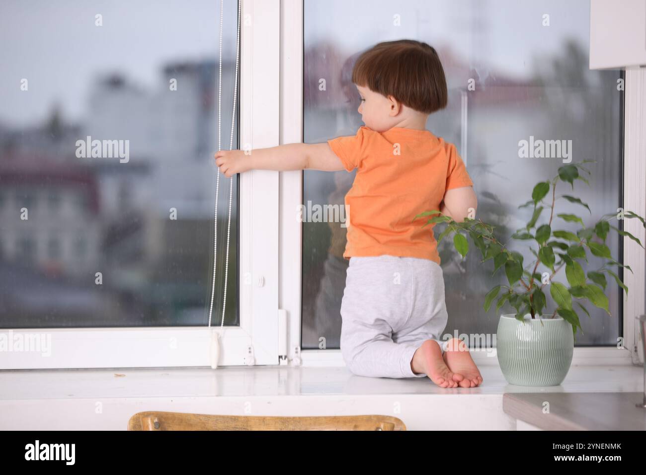 Little boy near window on windowsill, back view. Dangerous situation ...