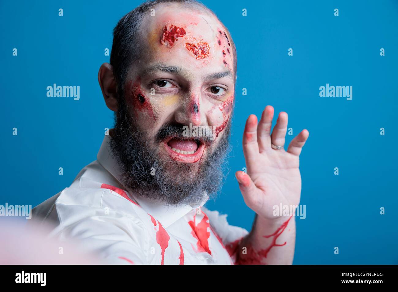 Portrait of man dressed as bloody zombie, turning hand into claw ...