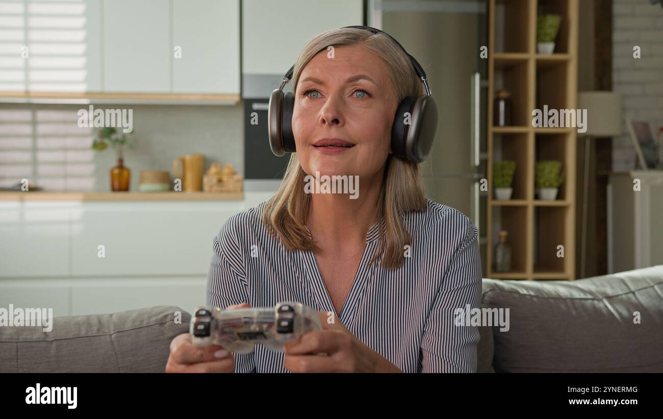 Funny smiling mature caucasian woman playing video game console in ...