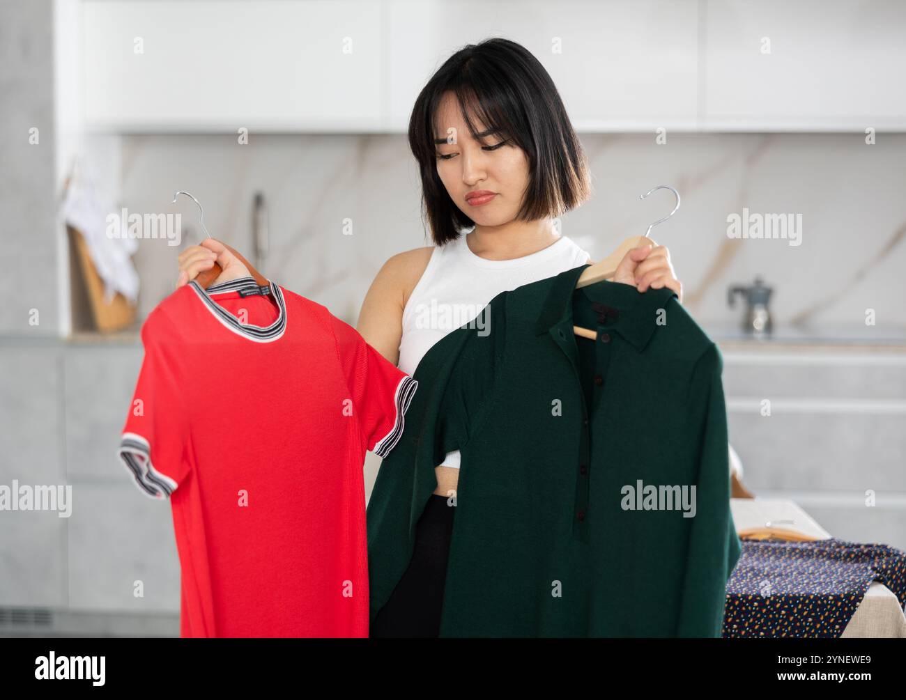Sad young Asian girl trying to choose a dress in the kitchen Stock ...