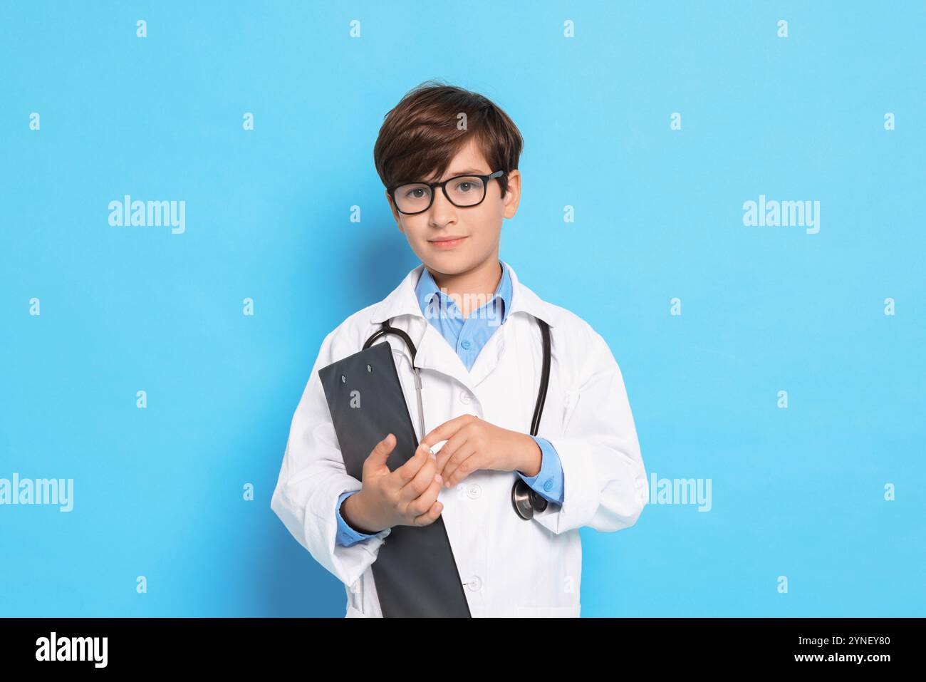 Boy with stethoscope and clipboard pretending to be doctor on light ...