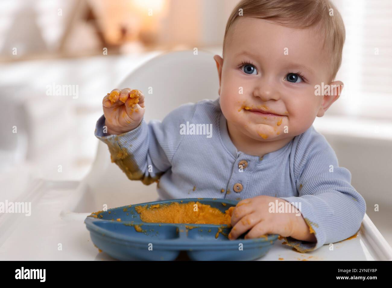 Cute little baby eating healthy food in high chair indoors Stock Photo ...