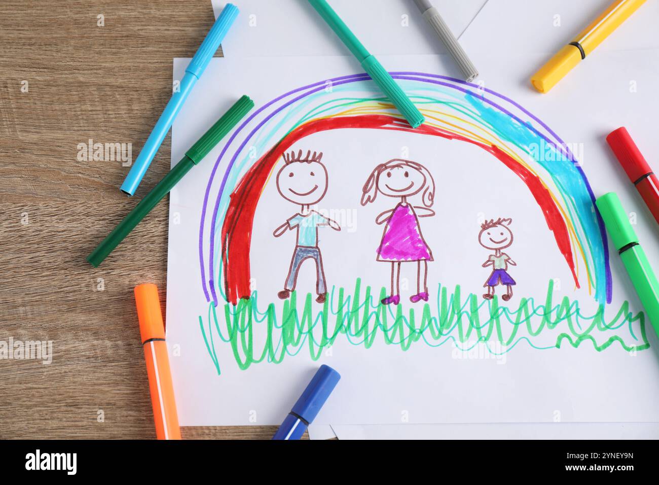 Child's drawing of happy family and felt tip pens on wooden table, top ...