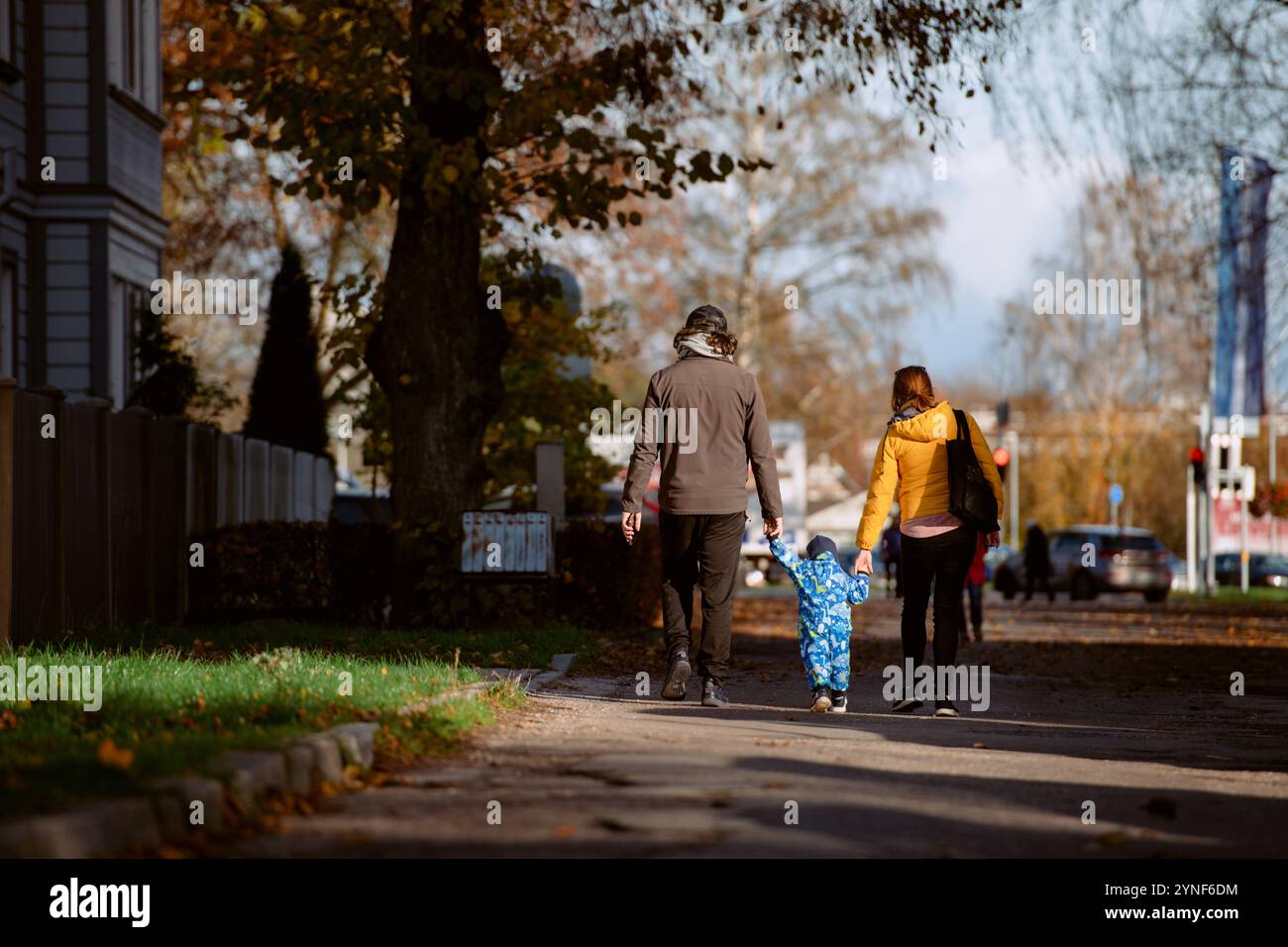 A loving couple strolls through a sunlit park with their young son ...