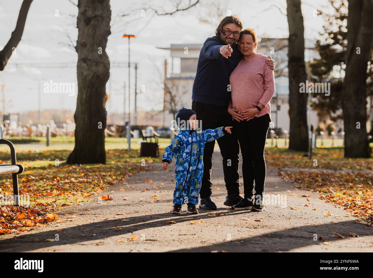 A loving couple strolls through a sunlit park with their young son ...