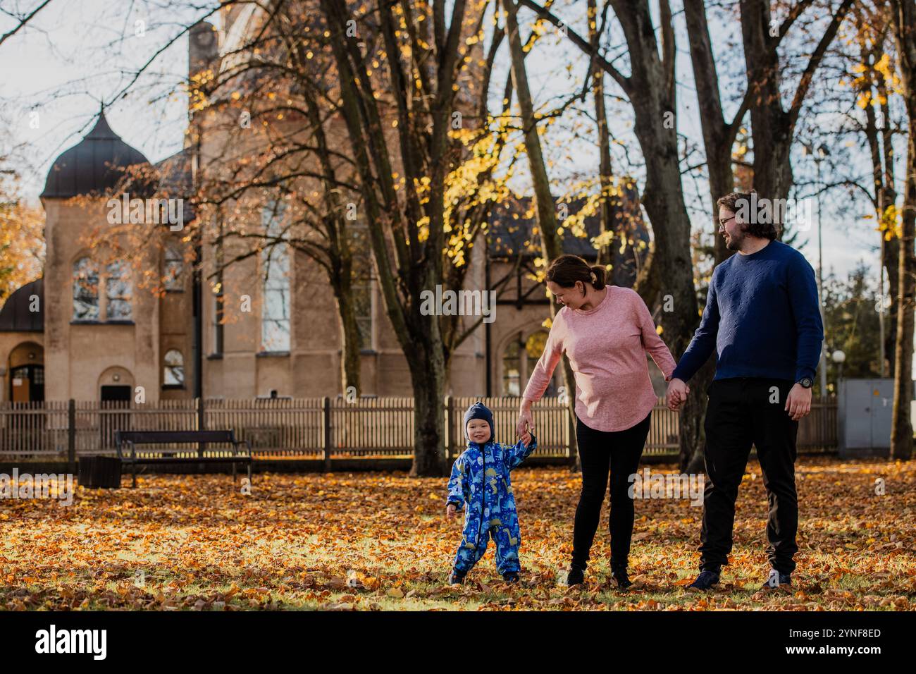 A loving couple strolls through a sunlit park with their young son ...