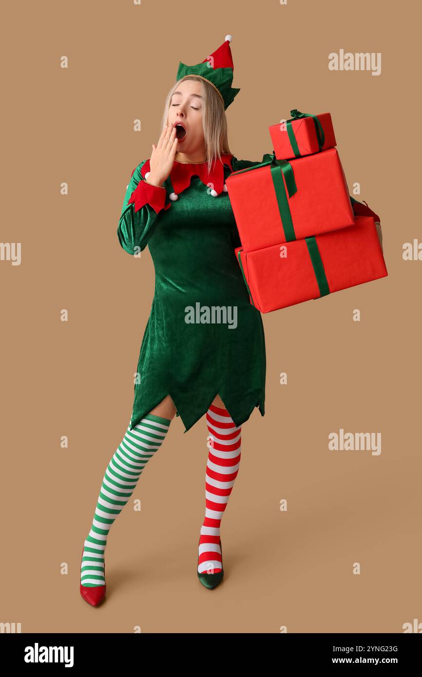 Young tired woman in elf costume holding Christmas gift boxes on brown ...