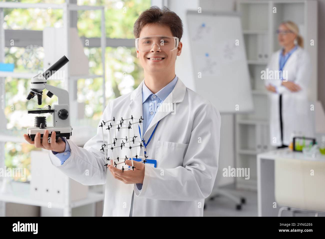 Male chemist with microscope and molecular model in laboratory Stock ...