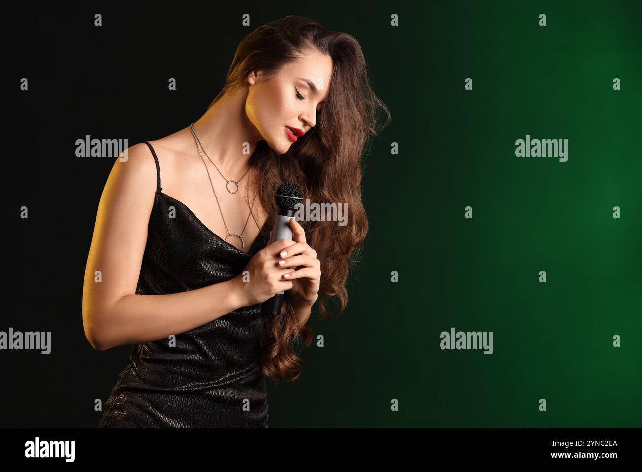 Female singer with microphone on dark green background Stock Photo - Alamy