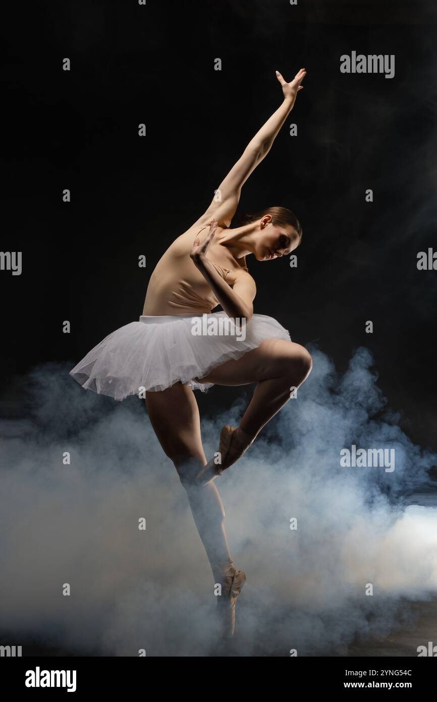 Dancer performing an elegant ballet pose amidst dramatic smoke effects ...