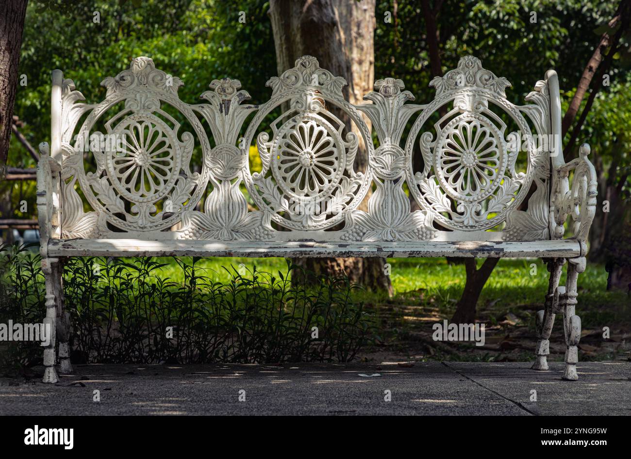 One empty bench made of white iron stands on city park. Sunlight on ...