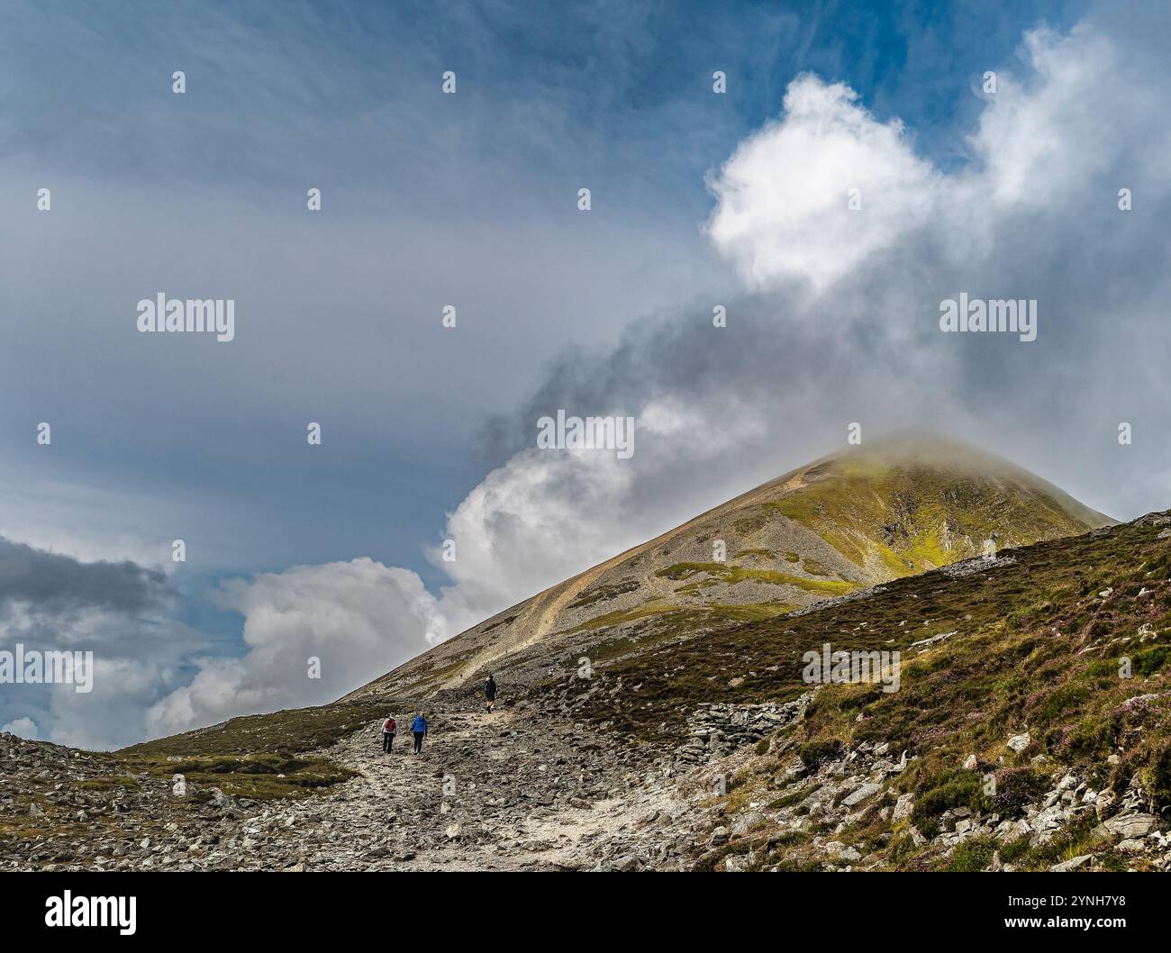 A group of hikers ascends a rocky mountain path under a vast, dramatic ...