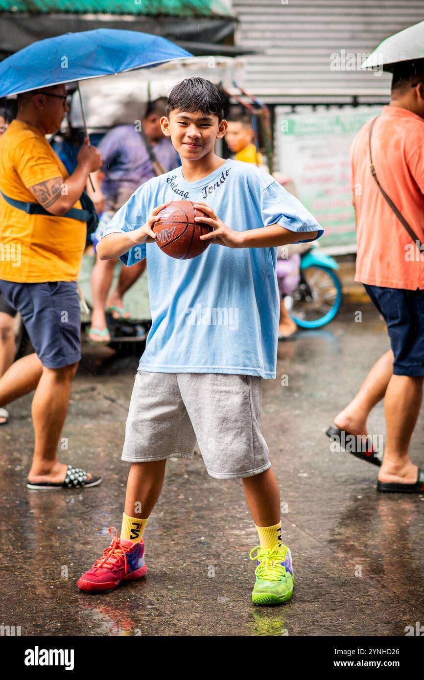 A young Filipino boy pauses whilst playing basketball standing on ...