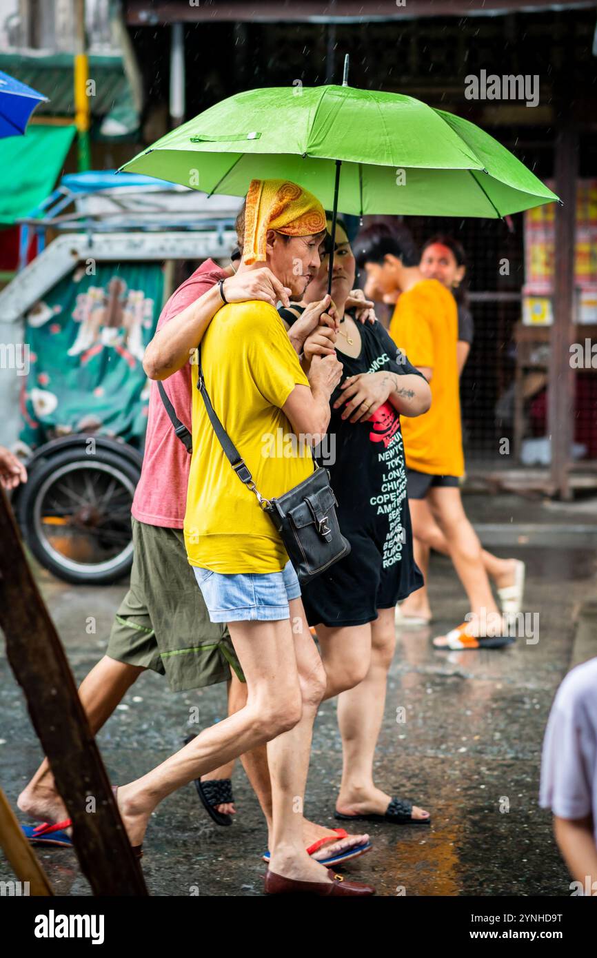 A group of Filipino people, holding an umbrella make their way along on ...