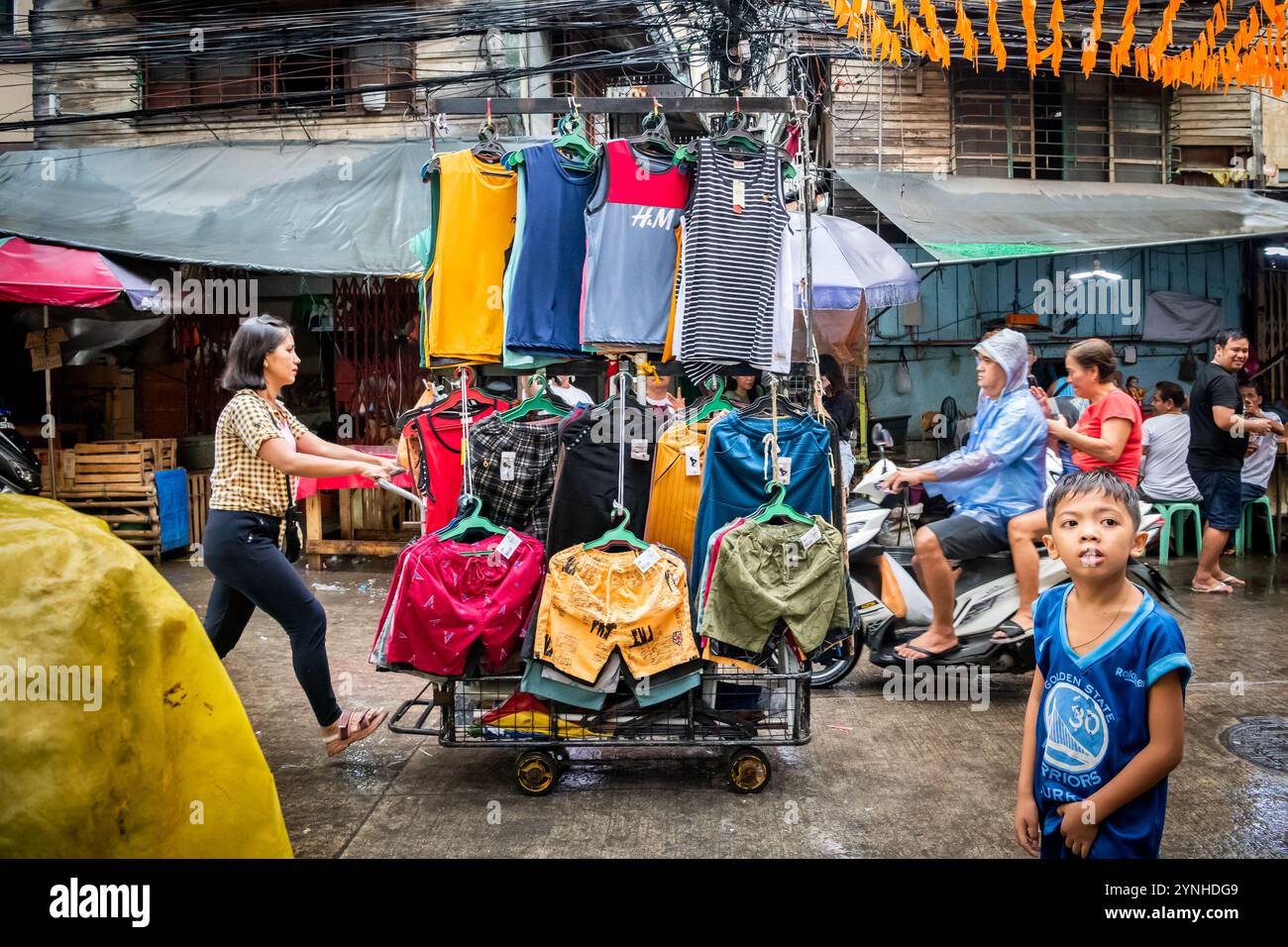 A lady pushes her mobile market stall selling clothes in a typical street in the Tondo District ...