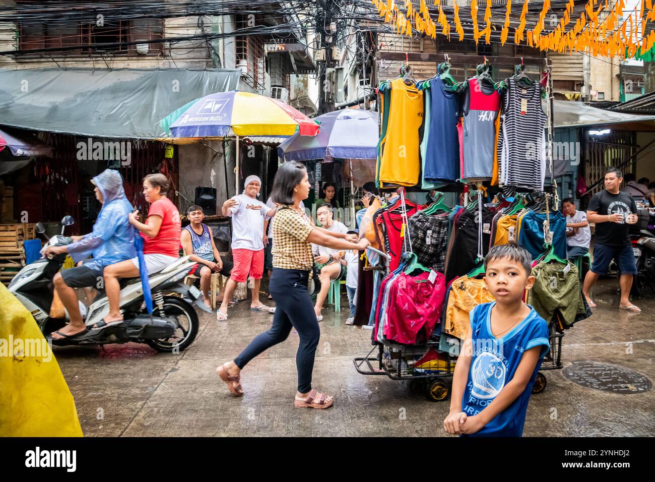 A lady pushes her mobile market stall selling clothes in a typical street in the Tondo District ...