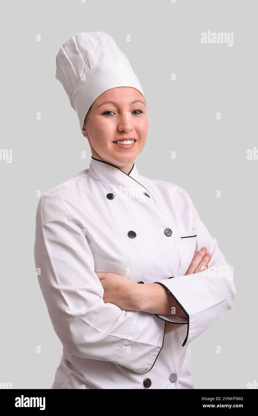 Young female chef smiling with arms crossed, wearing white uniform and ...