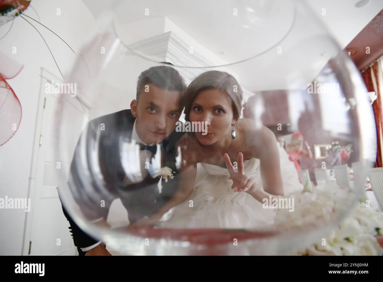 The bride and groom look at the camera through a glass. The image ...