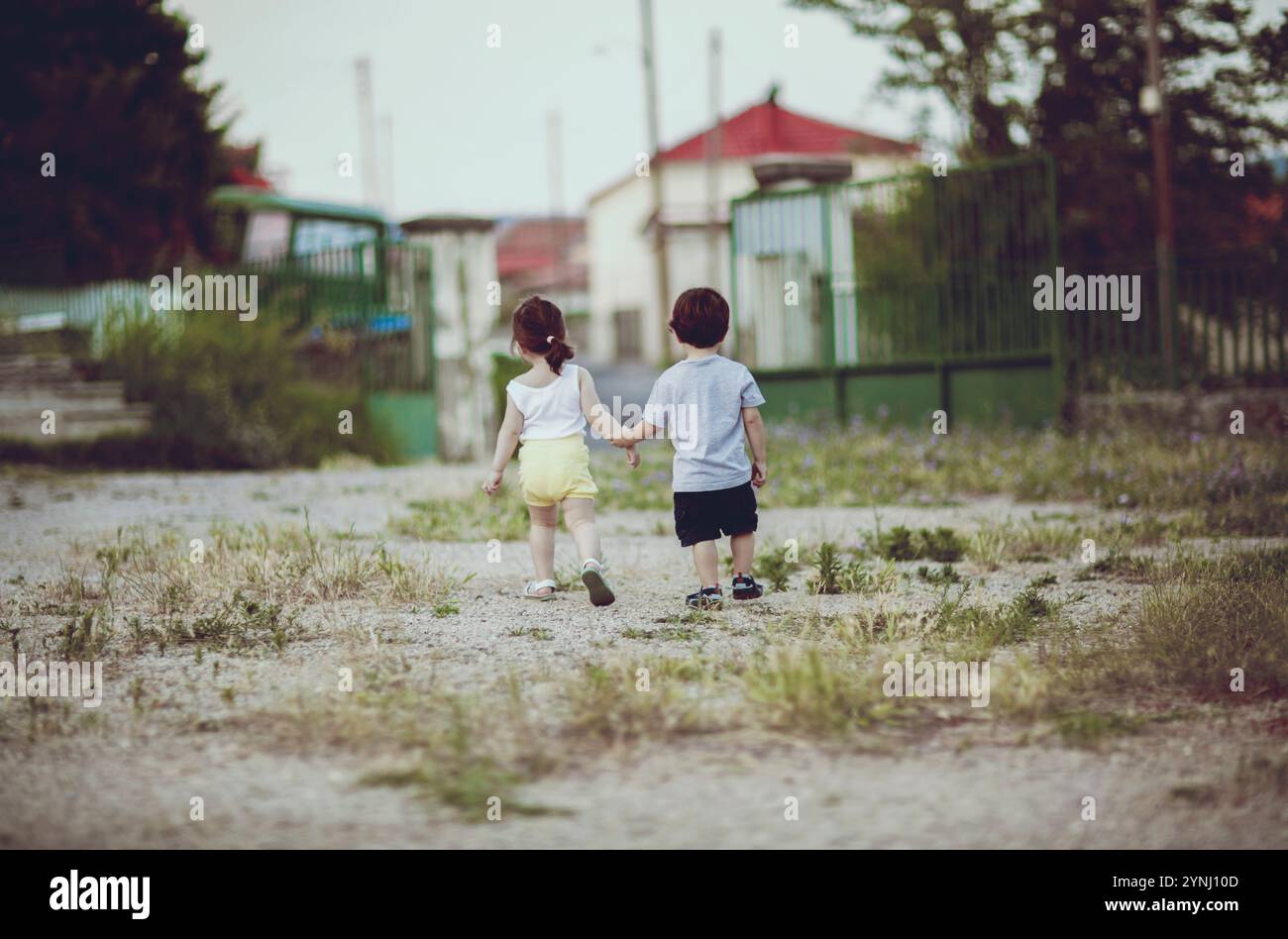Two children stroll together along a gravel path, holding hands and ...