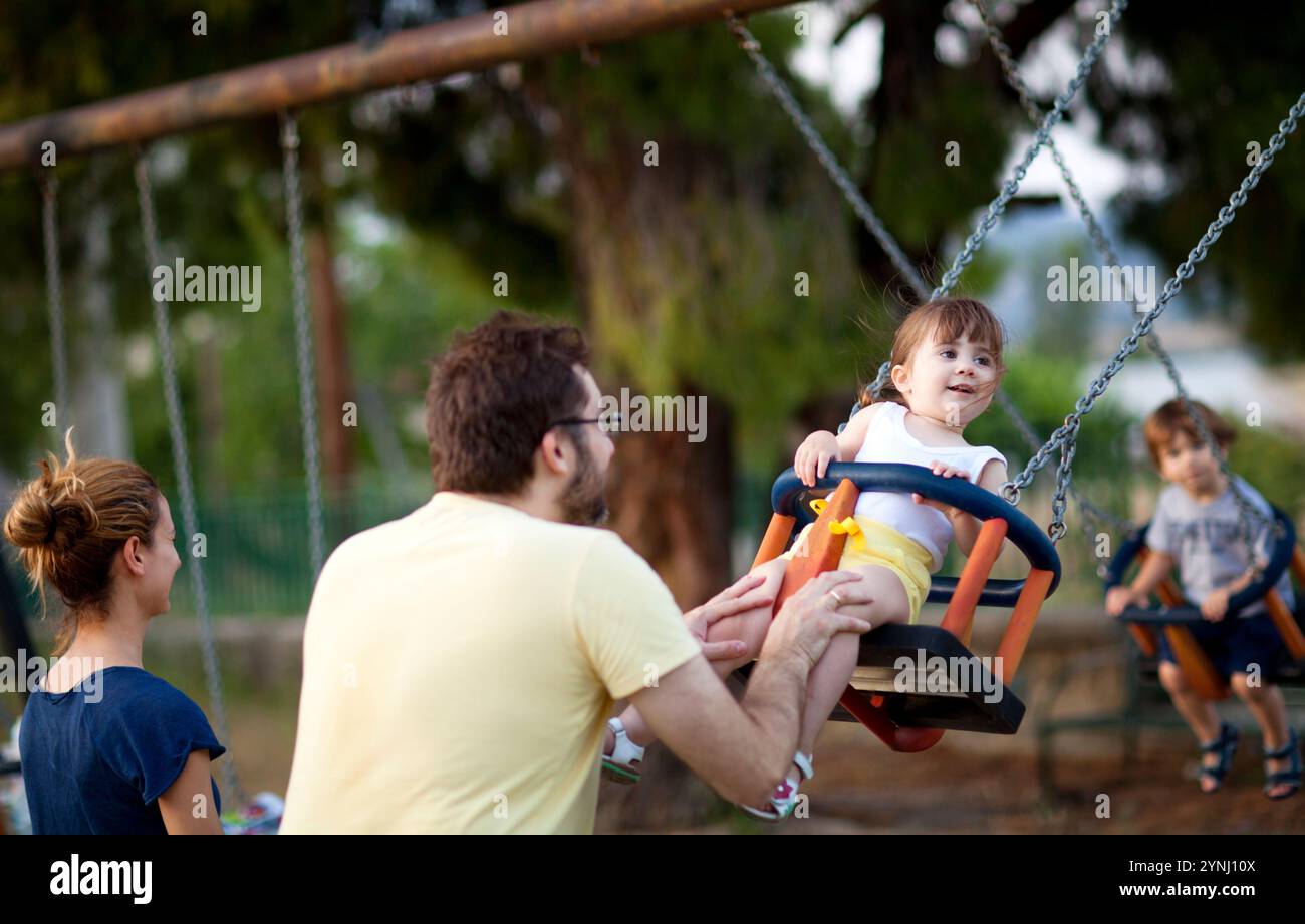 A family spends quality time at a playground, helping their young ...