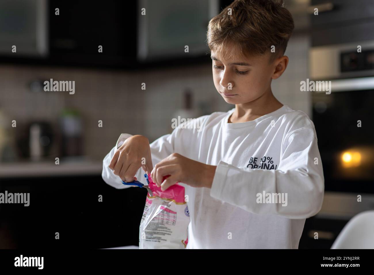 A young boy carefully opens a snack bag in a stylish kitchen. He ...