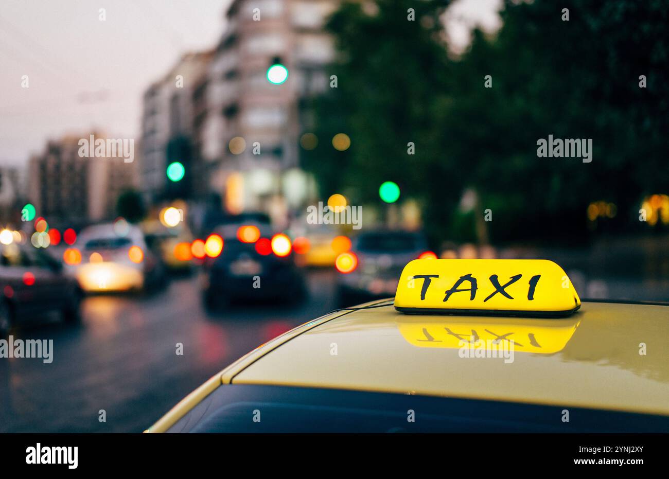 A yellow taxi waits in traffic on a bustling city road as dusk falls ...