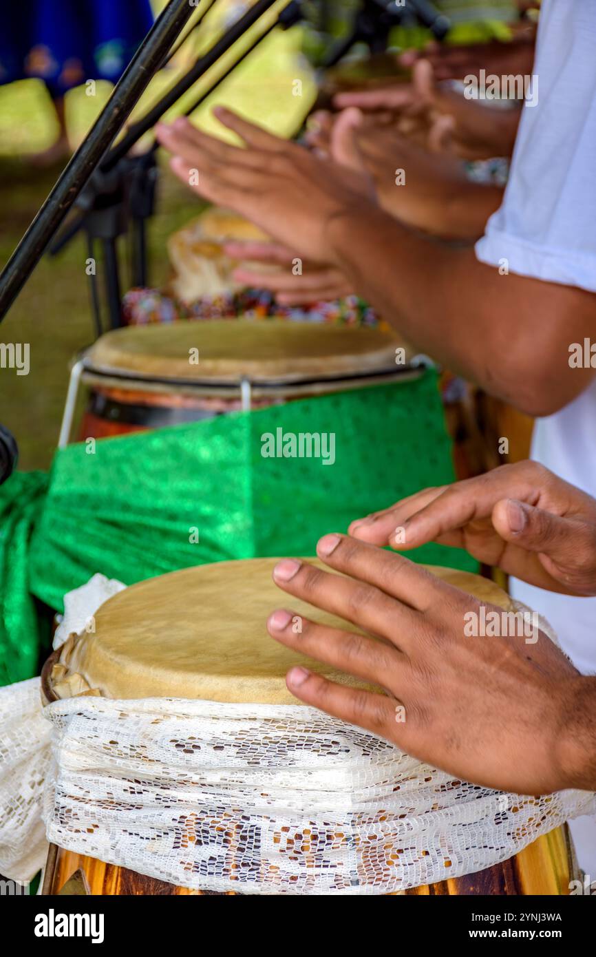Hands playing several atabaque drums decorated with fabric being used ...