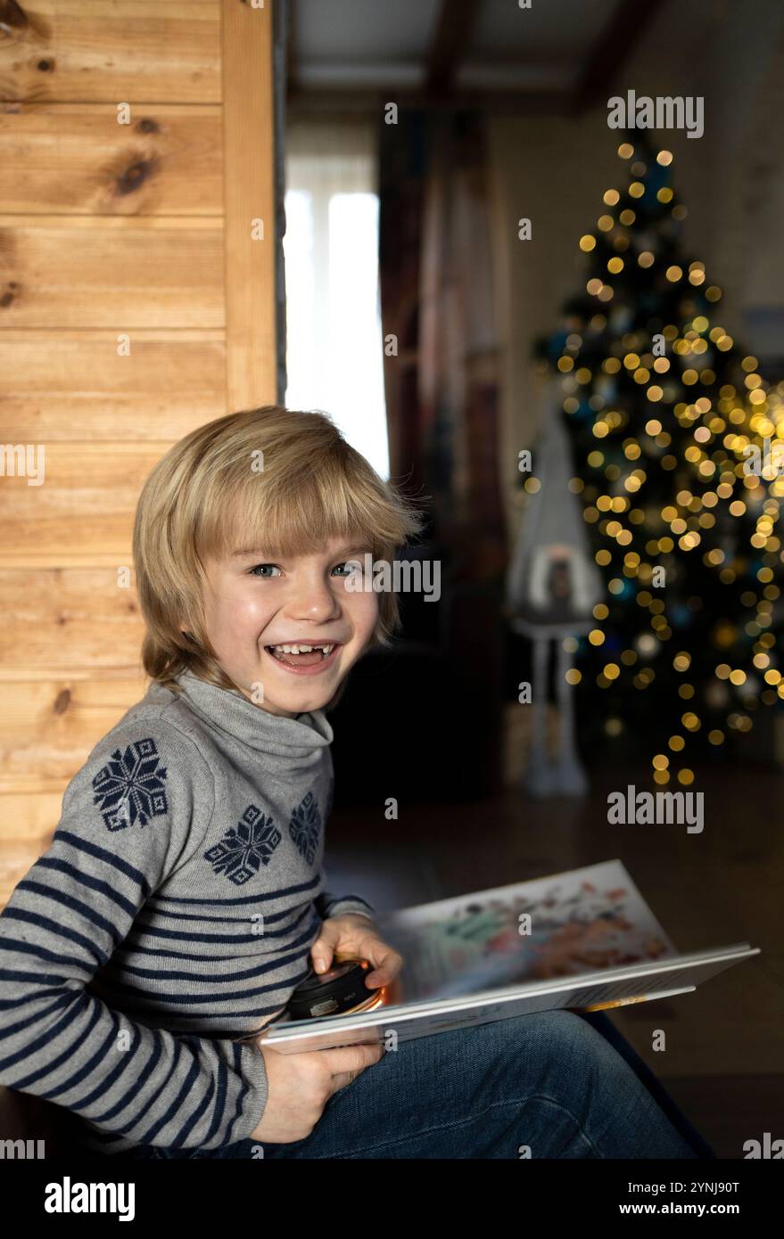 joyful toothless boy of 6-7 years old with an open book in his room ...