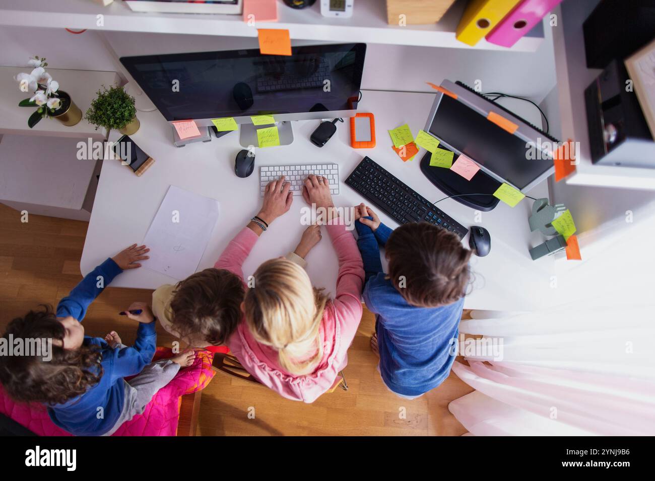 Three children and a parent focus on tasks at a home office desk ...